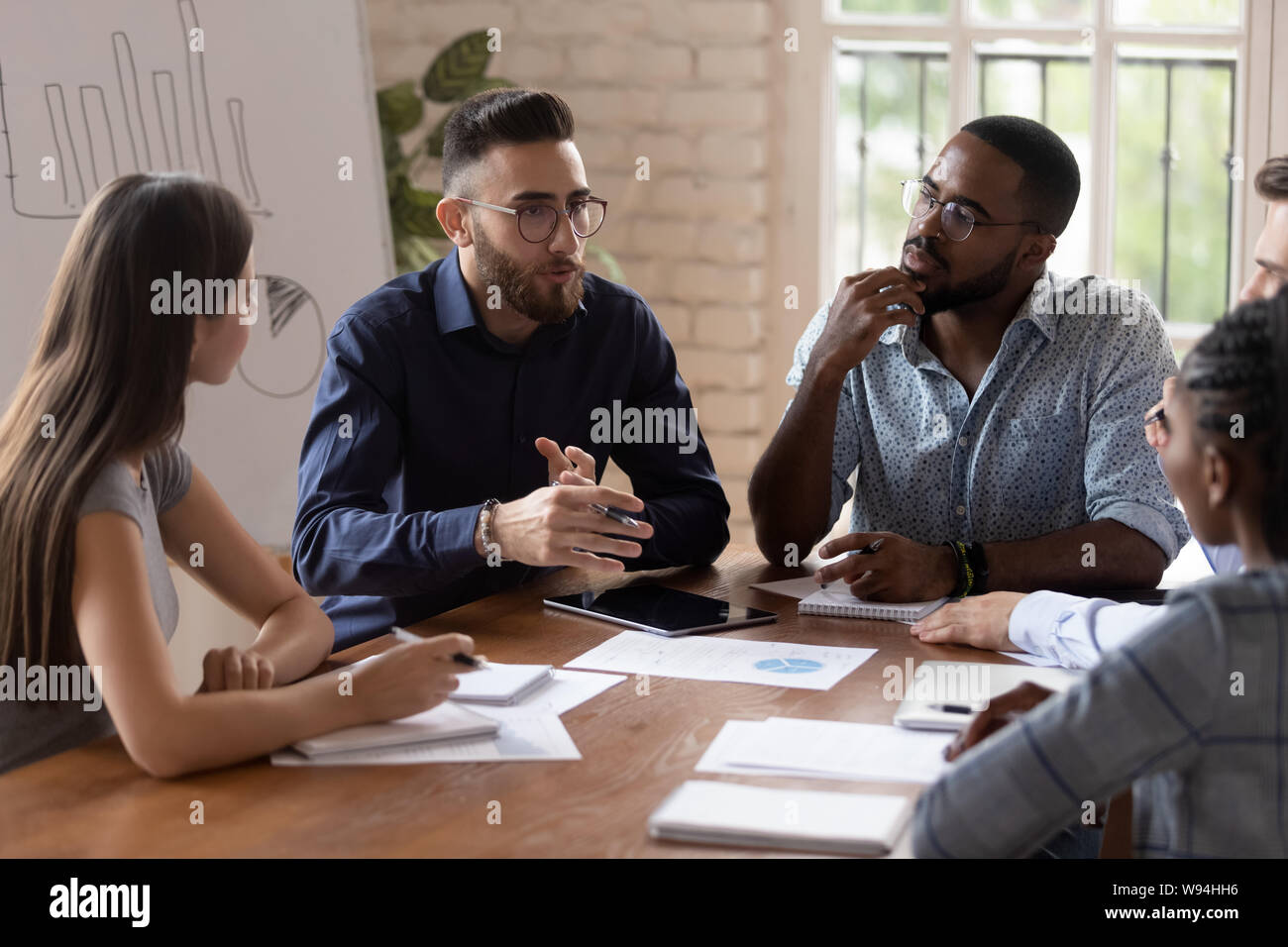 Serious businessman executive talk to diverse staff at briefing table ...