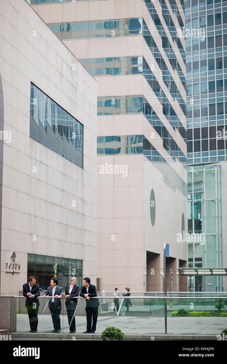Four businesspeople leaning on the railing of a walkway outside a ...
