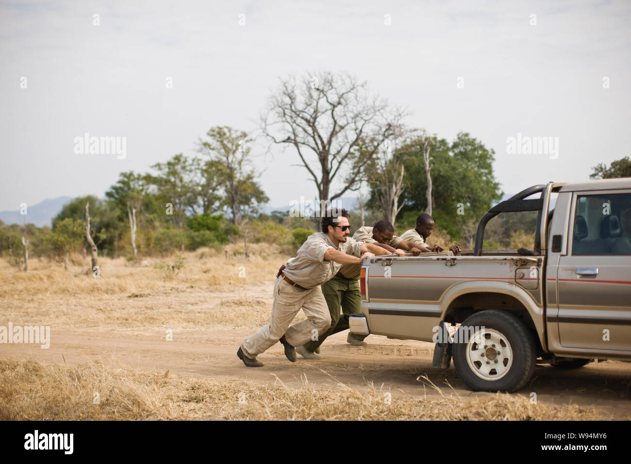 Three mid-adult men pushing a truck along a dirt road Stock Photo - Alamy