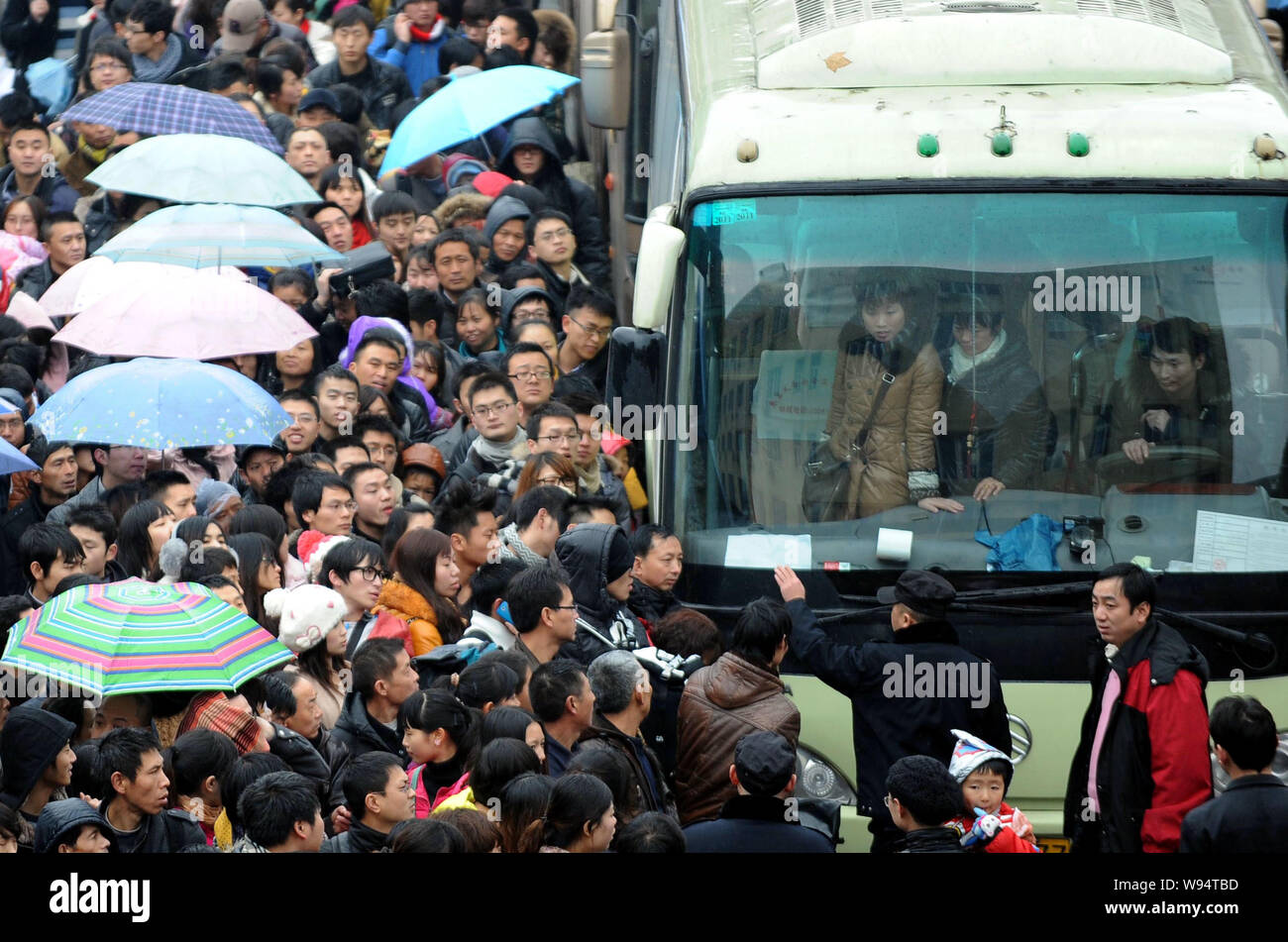 A crowd of passengers queue to board buses at a long-distance bus ...