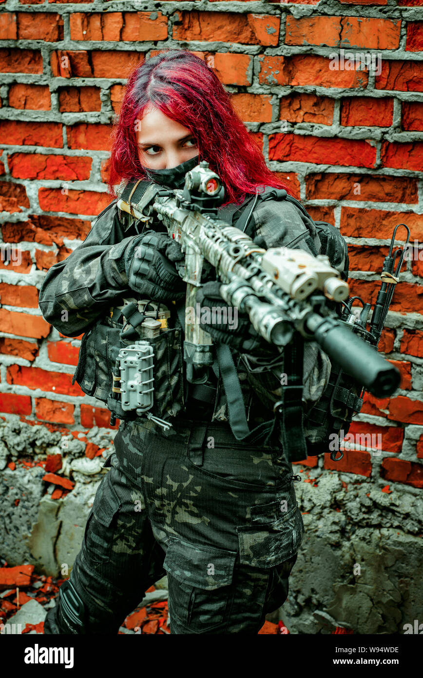 Red-hair woman in military uniform with machine gun on bricks wall ...