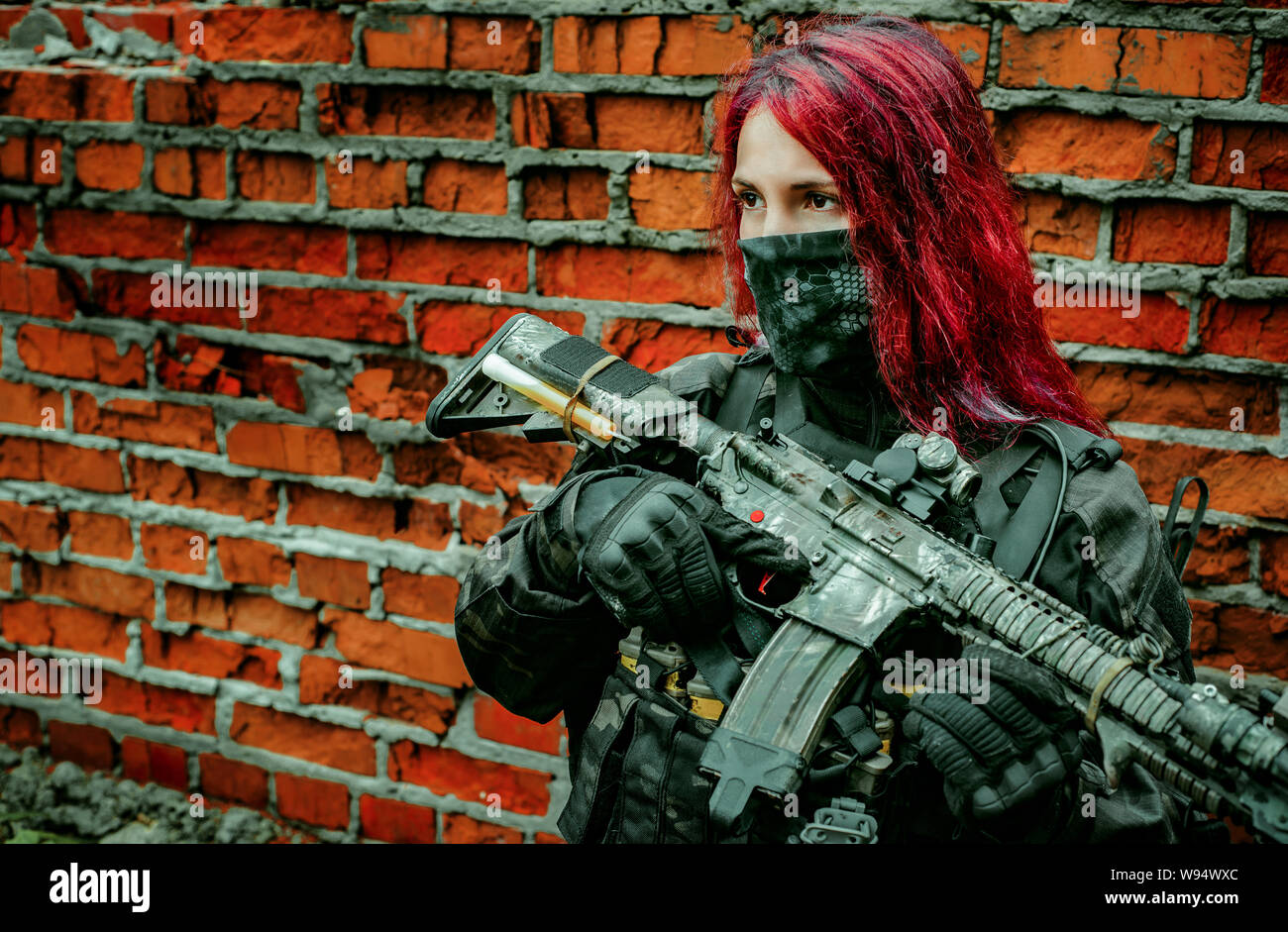 Red-hair woman in military uniform with machine gun on bricks wall ...
