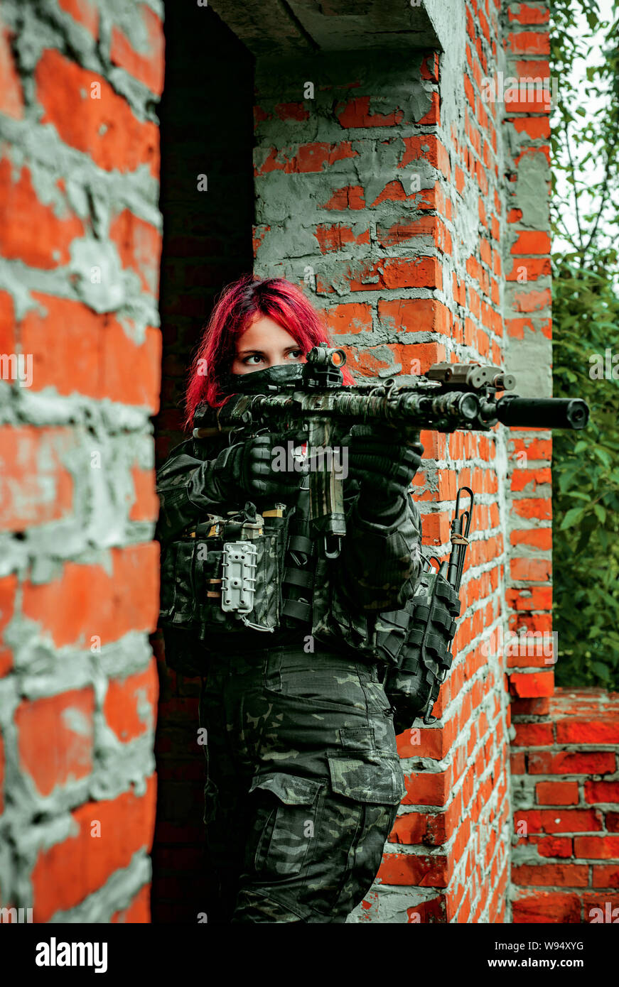 Red-hair woman in military uniform with machine gun beside bricks wall ...