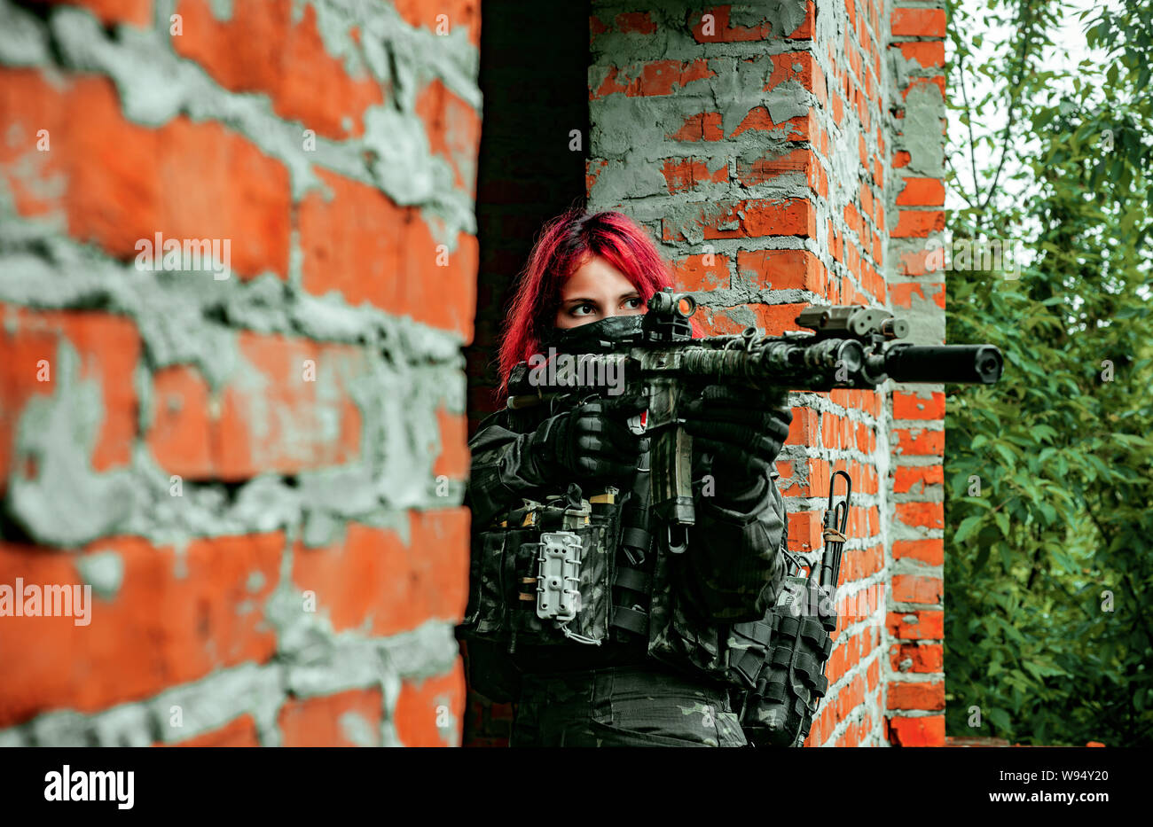 Red-hair woman in military uniform with machine gun beside bricks wall ...
