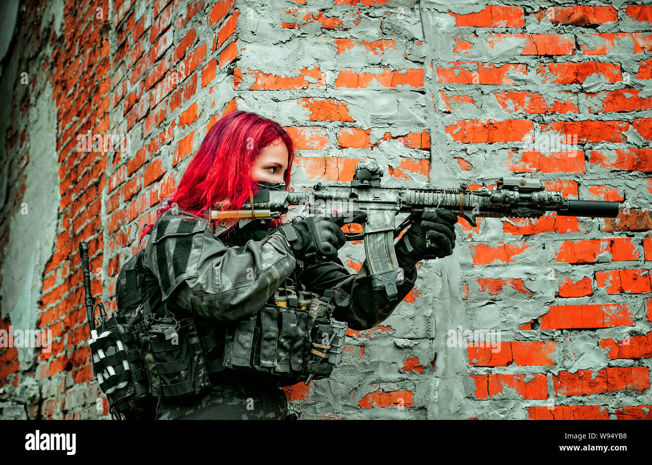 Red-hair woman in military uniform with machine gun beside bricks wall ...