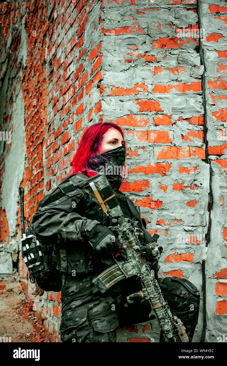 Red-hair woman in military uniform with machine gun beside bricks wall ...