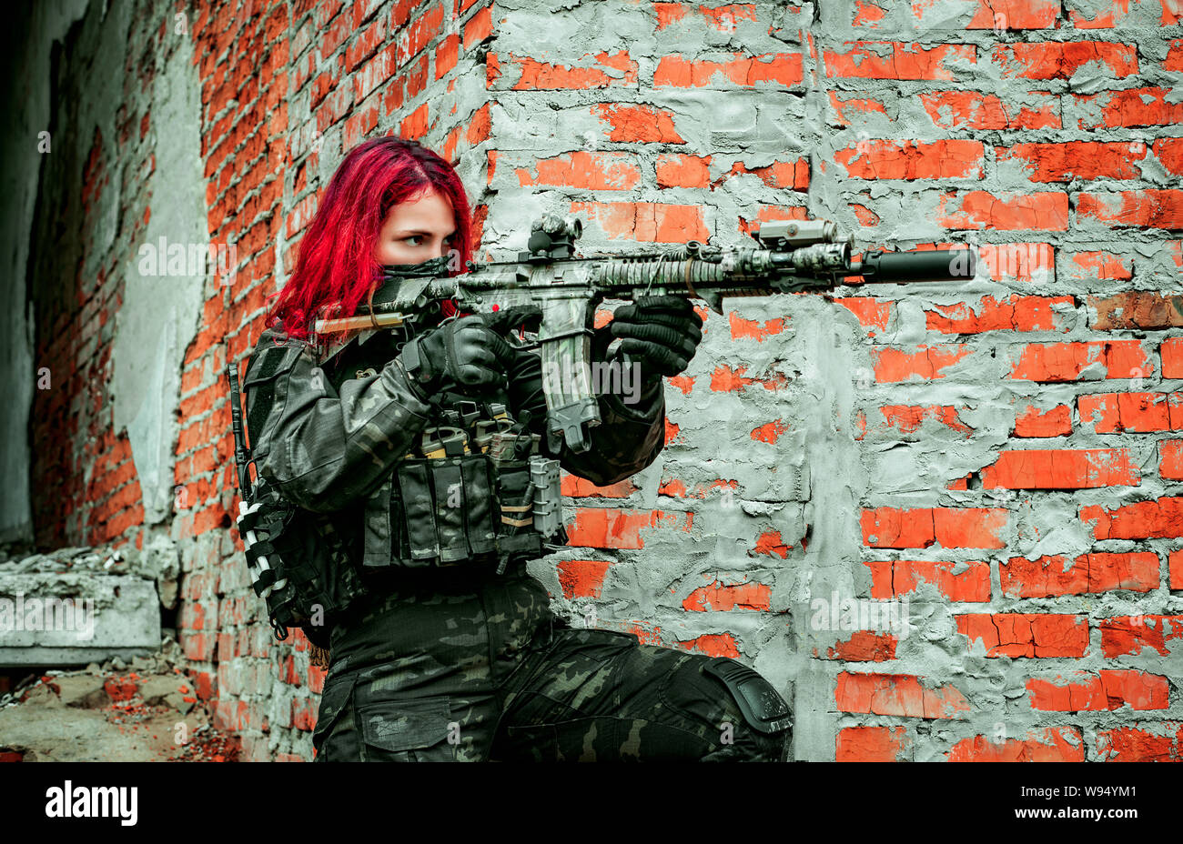 Red-hair woman in military uniform with machine gun beside bricks wall ...
