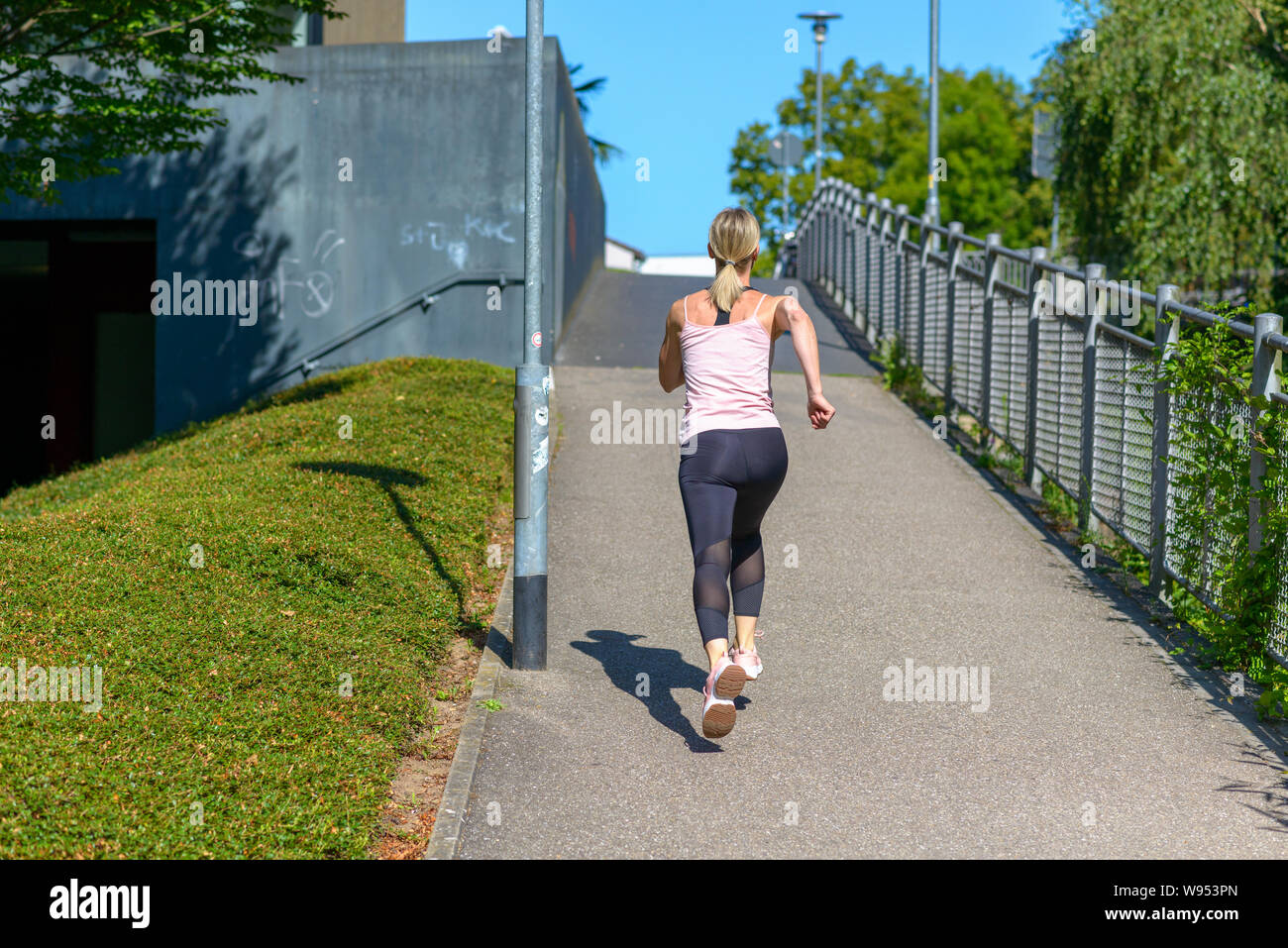 Fit woman jogging up a steep urban hill along a walkway during her ...