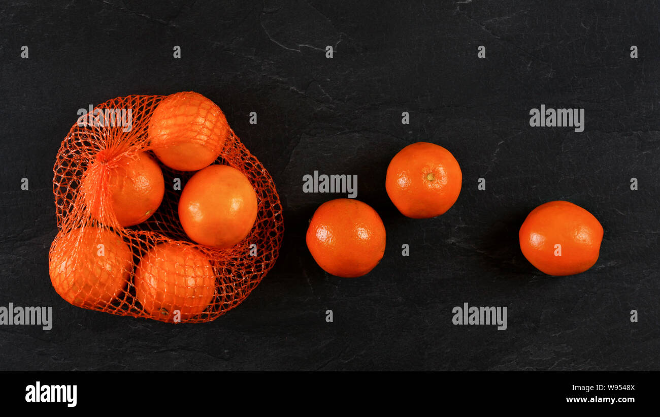 Oranges in net, some scattered on black stone like board, flat lay ...