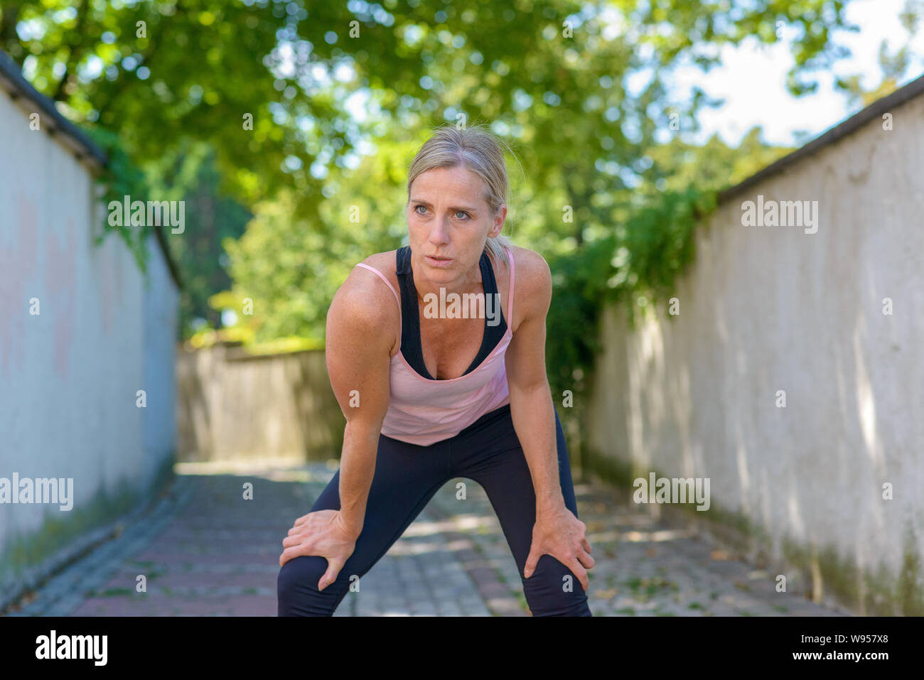 Fit muscular woman resting during a workout bending forwards with hands ...