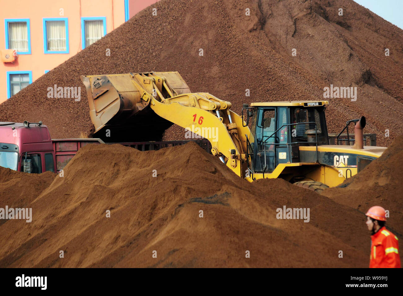 --FILE--A Chinese worker walks past a wheel loader loading a truck with ...