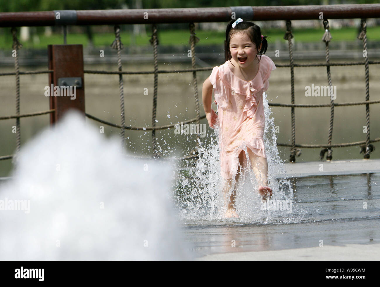 A young girl plays with water to cool herself off in a fountain on a ...