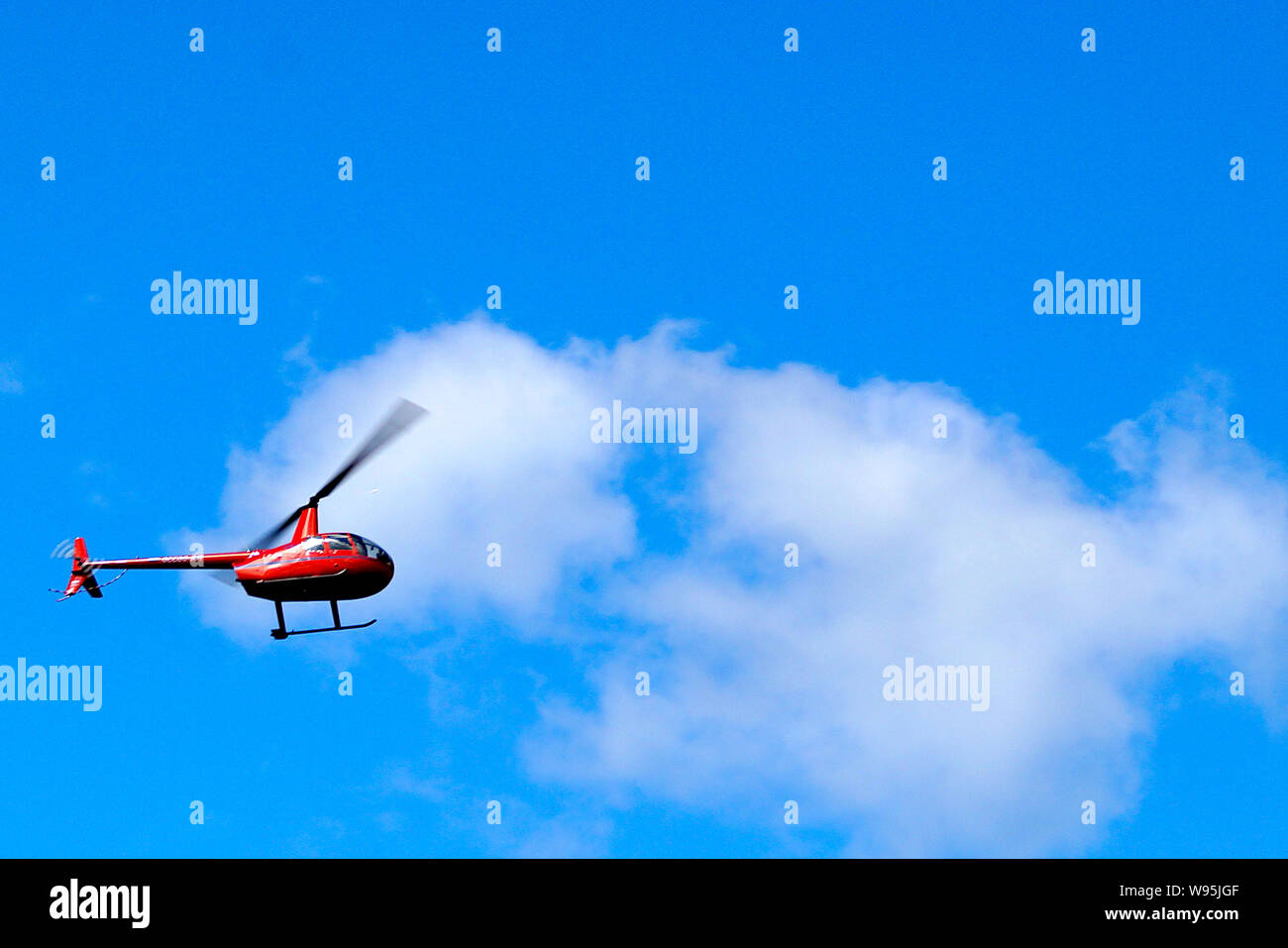 A small red helicopter flies through the blue sky with white clouds ...