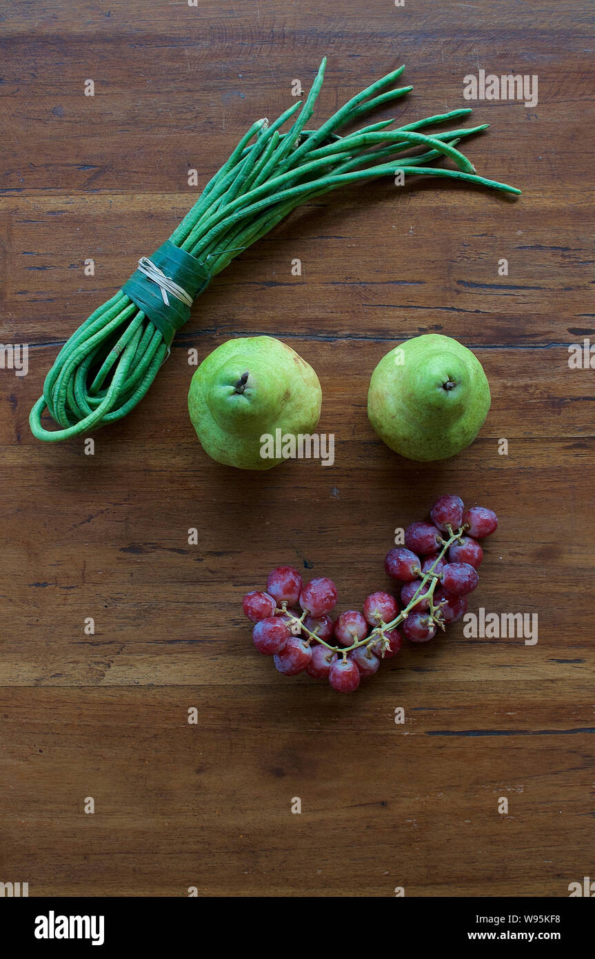 A smiling face made out of different fruits and vegetables on a wooden ...
