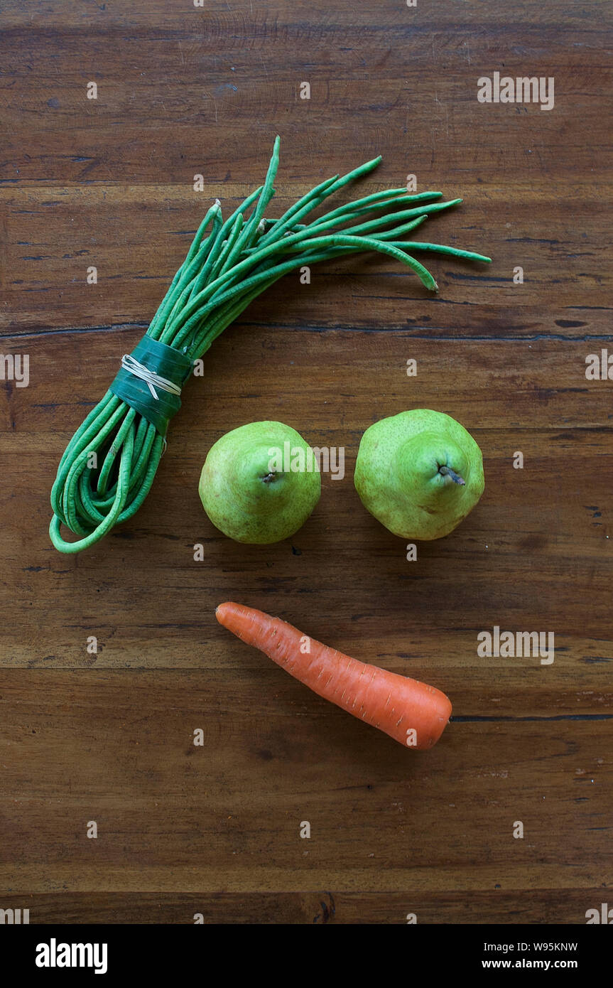 A confused face made out of different fruits and vegetables on a wooden ...