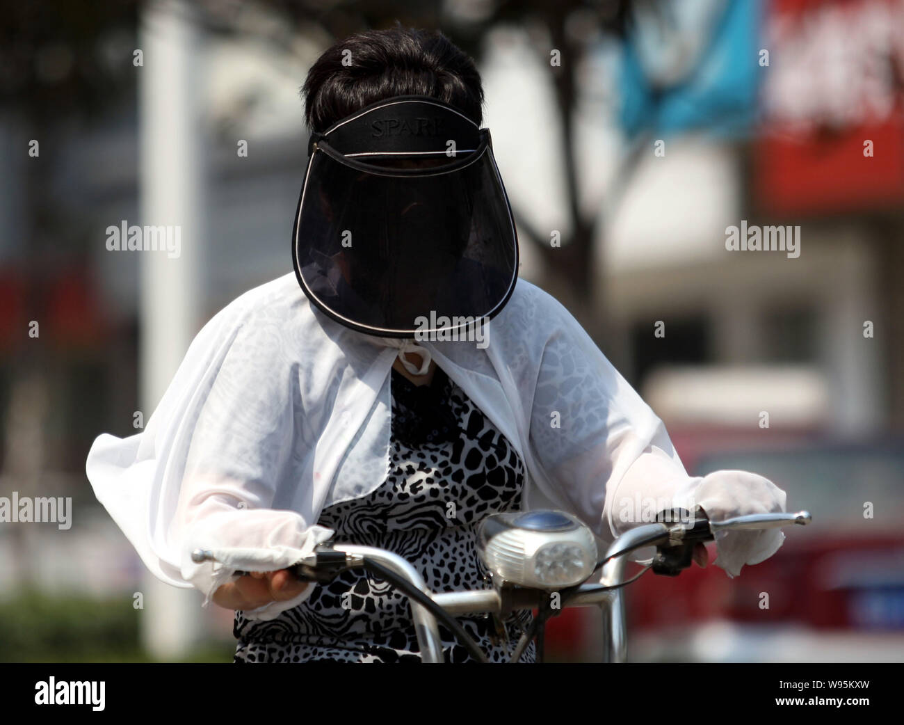 A cyclist shielding her face with a cap from scorching sunshine rides ...