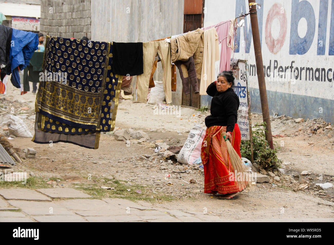 Woman in traditional dress sweeping litter on street near drying ...