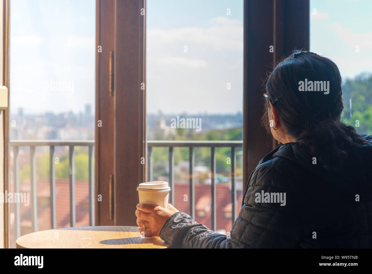 Single elder woman sit in cafe beside windows, hold a white cup of ...