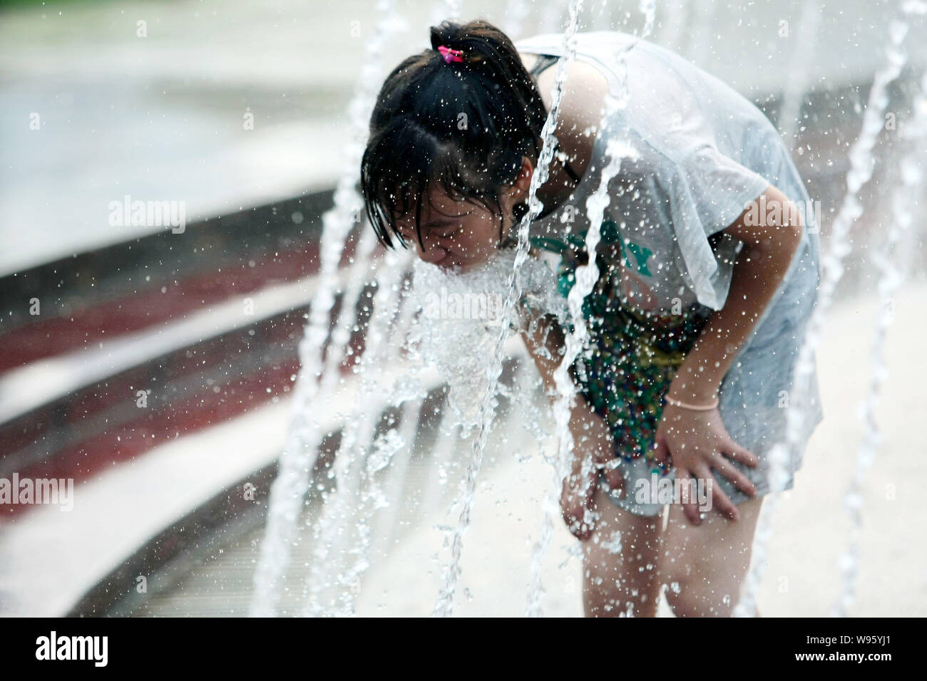 A young girl plays with water to cool herself off in a fountain on a ...