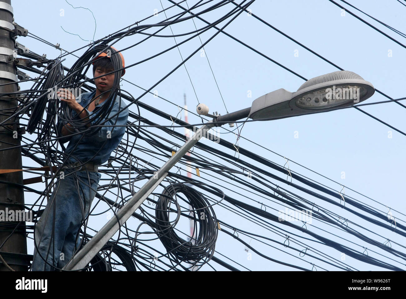 A Chinese electrician checks and repairs electrical wires on a pole in ...