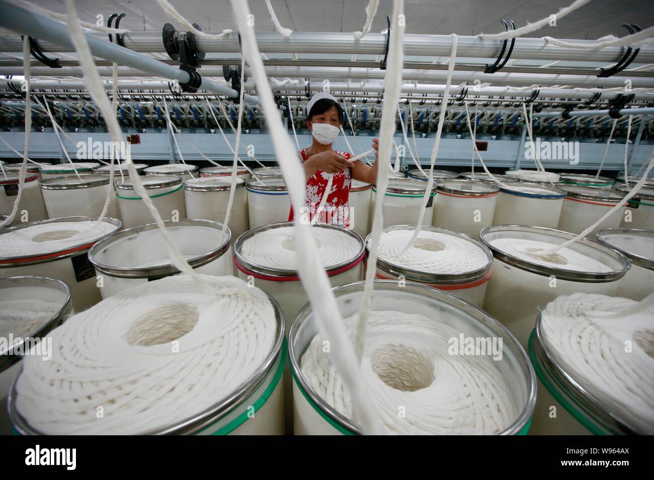 A female Chinese worker handles the production of yarn on the spinning machine at a textile ...