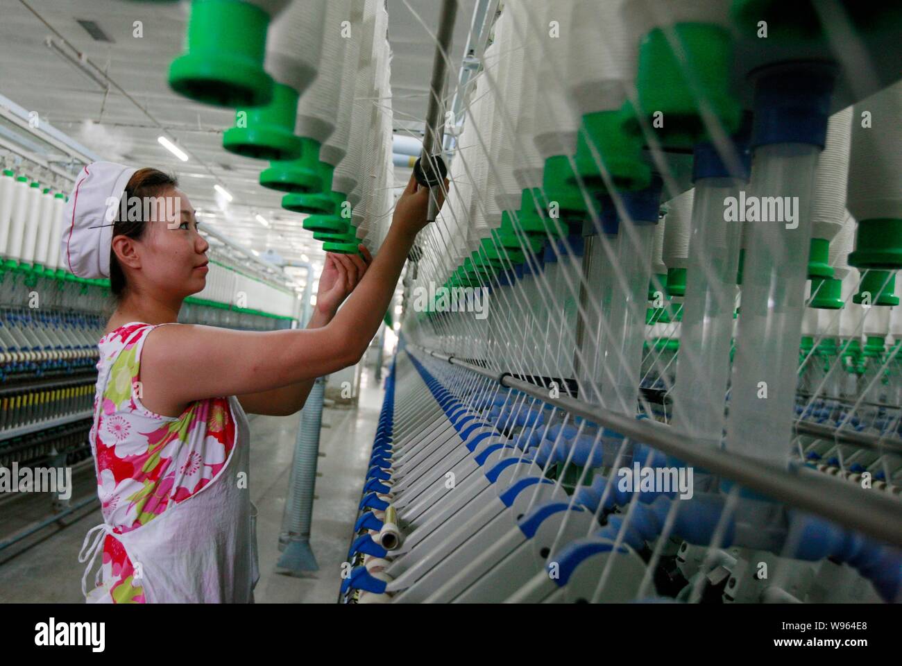 A female Chinese worker handles the production of yarn on the spinning machine at a textile ...