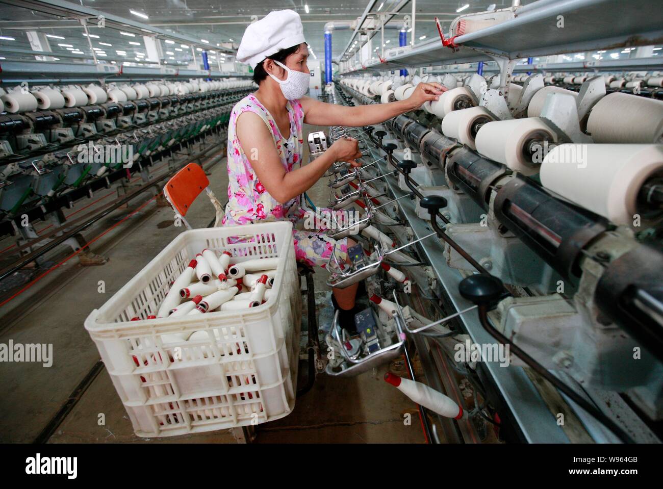 A female Chinese worker handles the production of yarn on the spinning machine at a textile ...