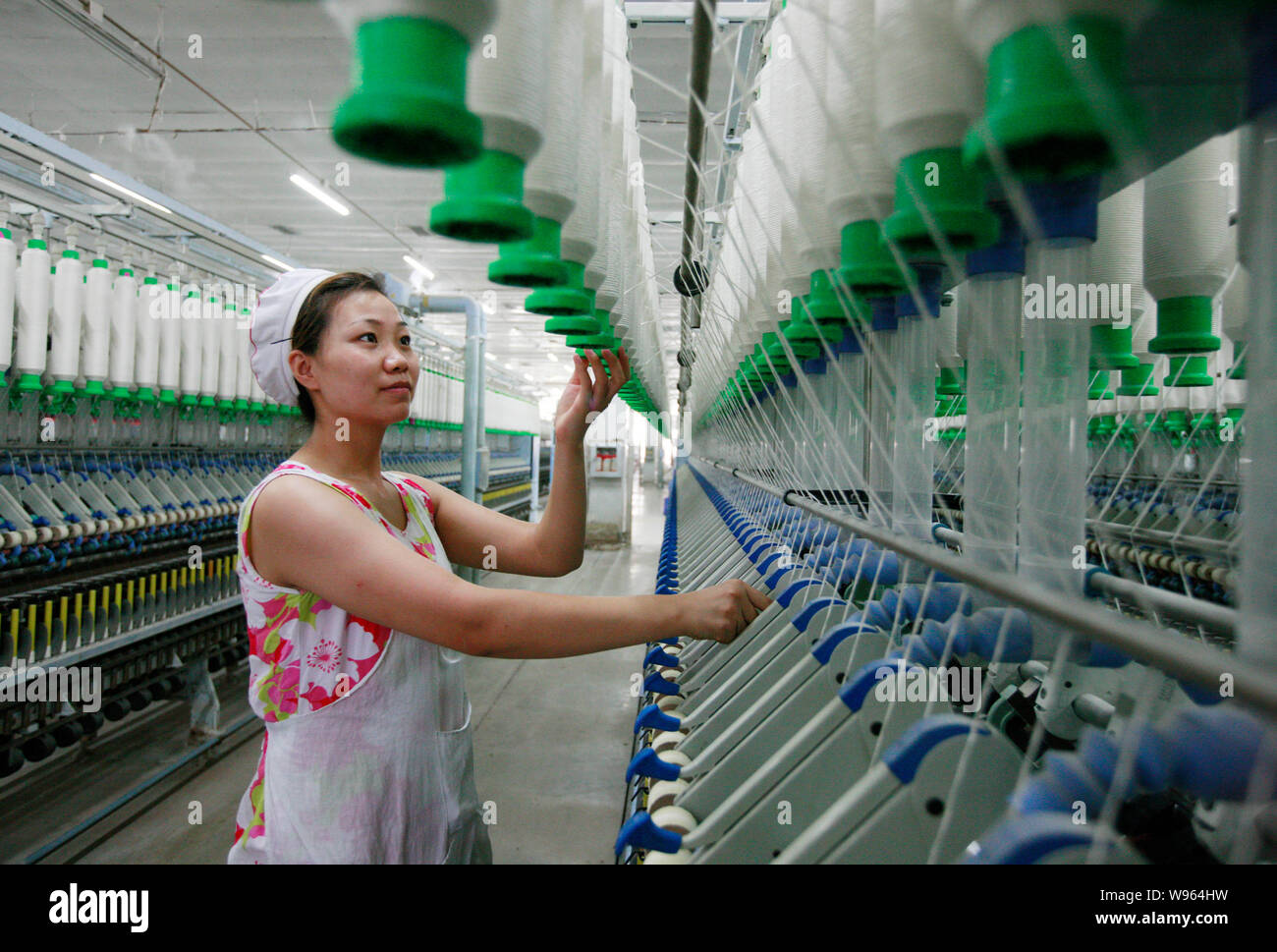 A female Chinese worker handles the production of yarn on the spinning machine at a textile ...