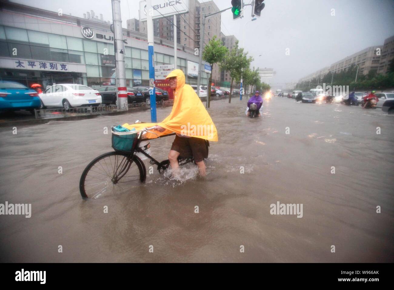 Cyclists and vehicles brave floods on a road in heavy rain caused by ...