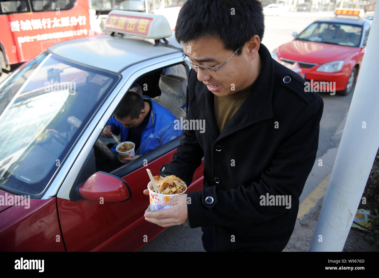 A taxi driver eats instant noodles besides a long queue of taxis to be ...
