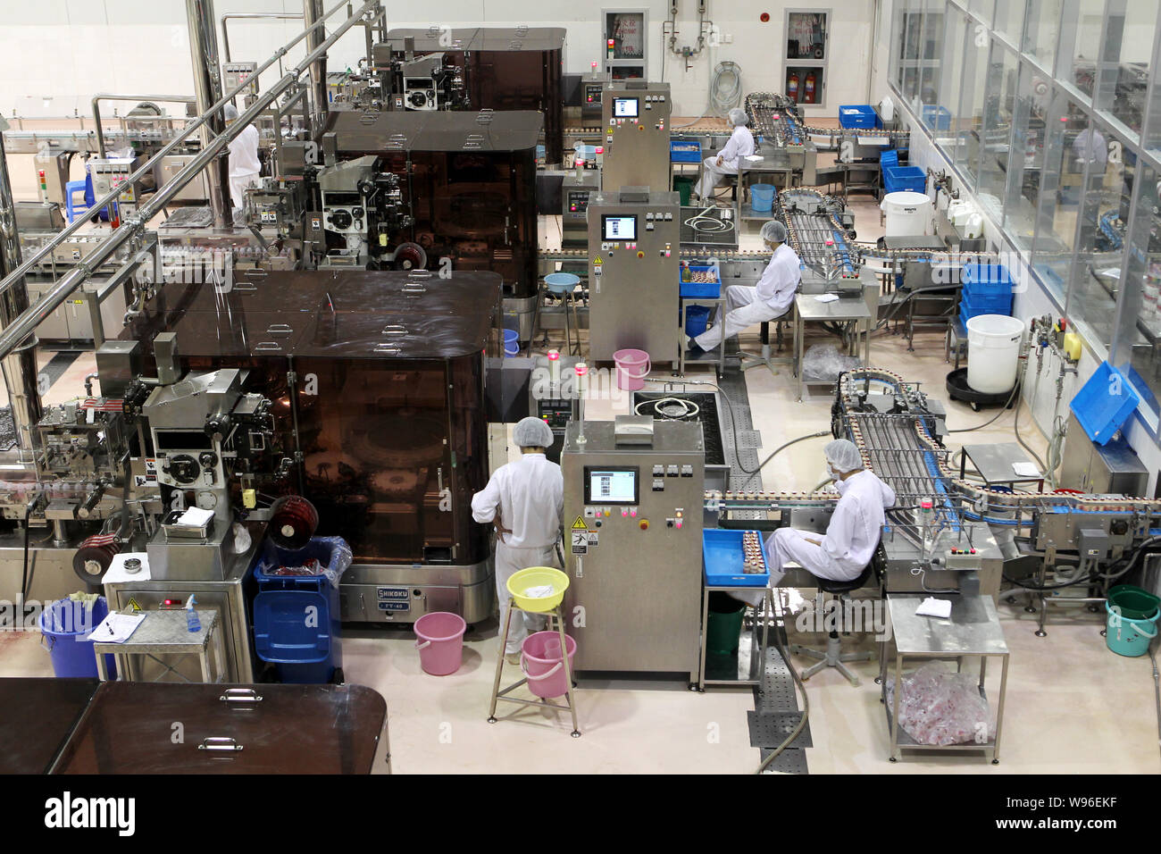 Factory workers watch bottles of Yakult fermented milk drink passing ...