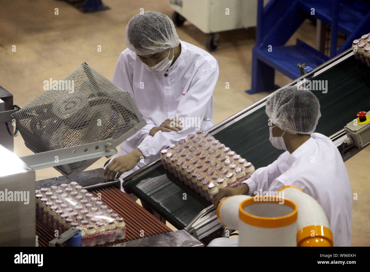 Factory workers watch bottles of Yakult fermented milk drink passing ...