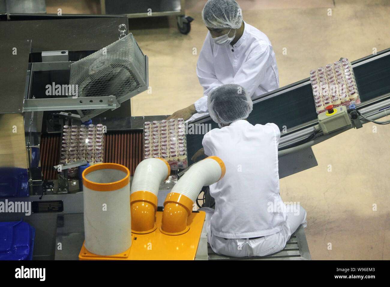 Factory workers watch bottles of Yakult fermented milk drink passing ...