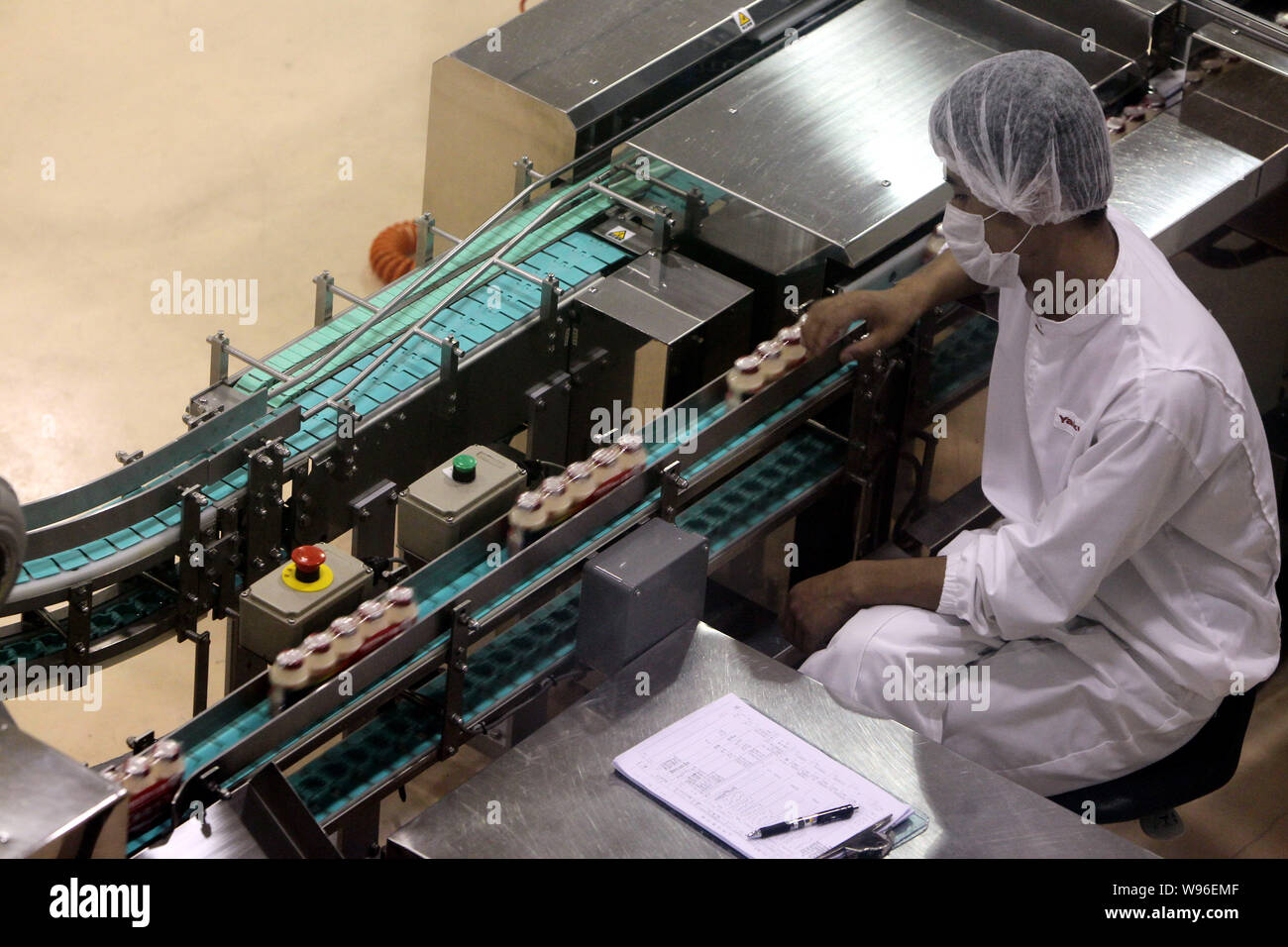 A factory worker watches bottles of Yakult fermented milk drink passing ...