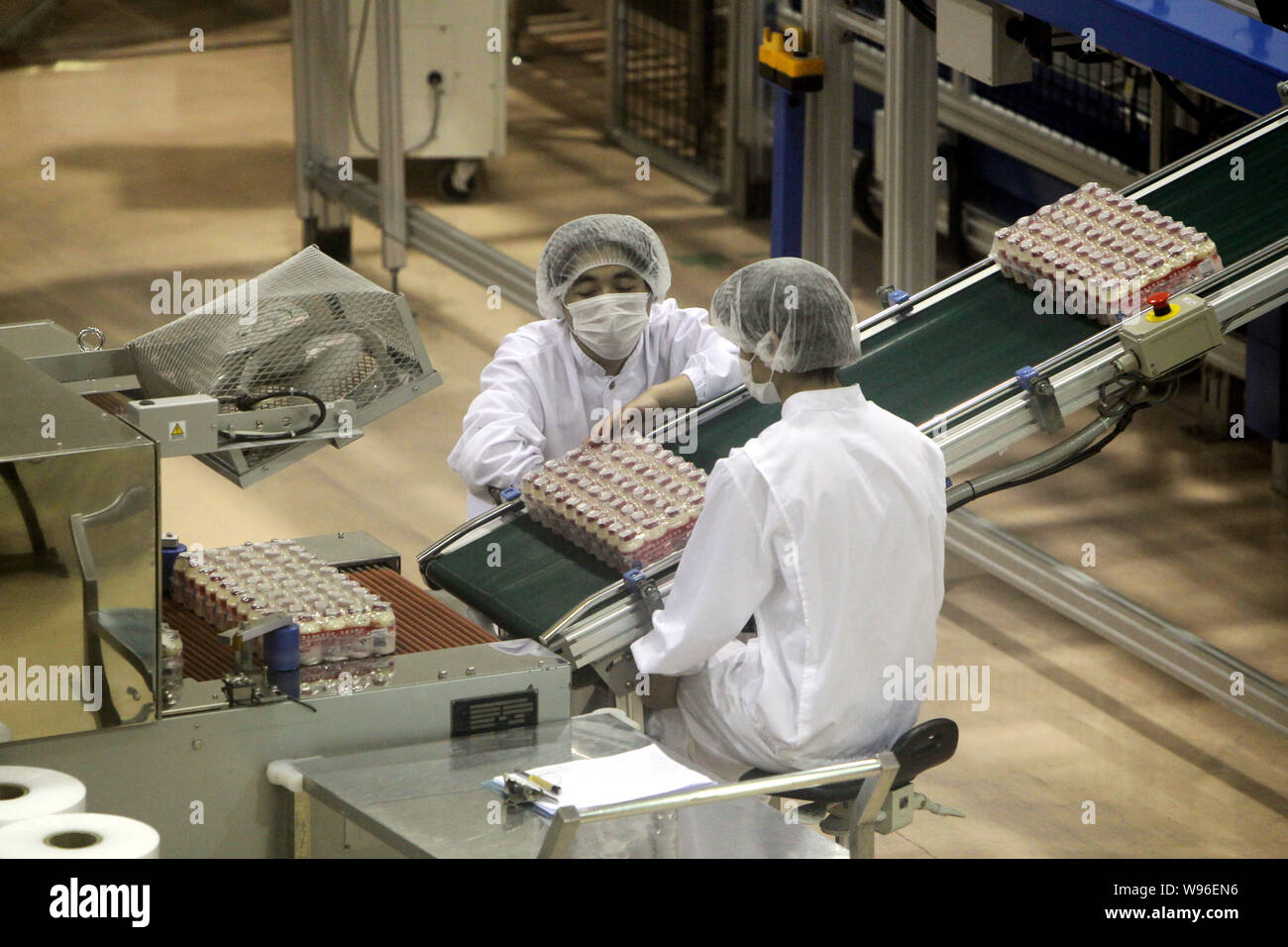 Factory workers watch bottles of Yakult fermented milk drink passing ...