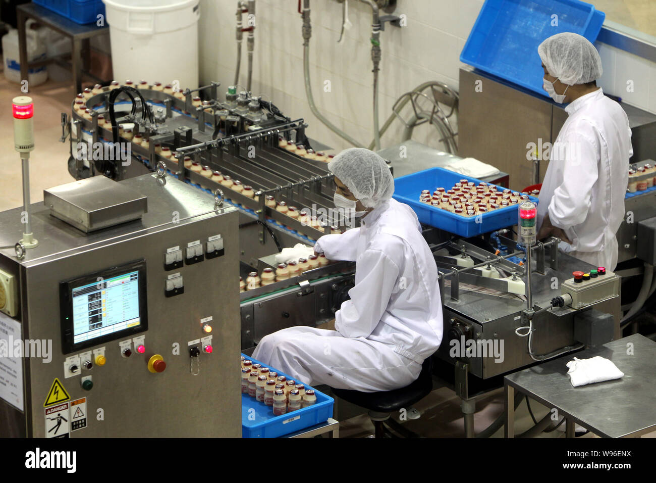 Factory workers watch bottles of Yakult fermented milk drink passing ...