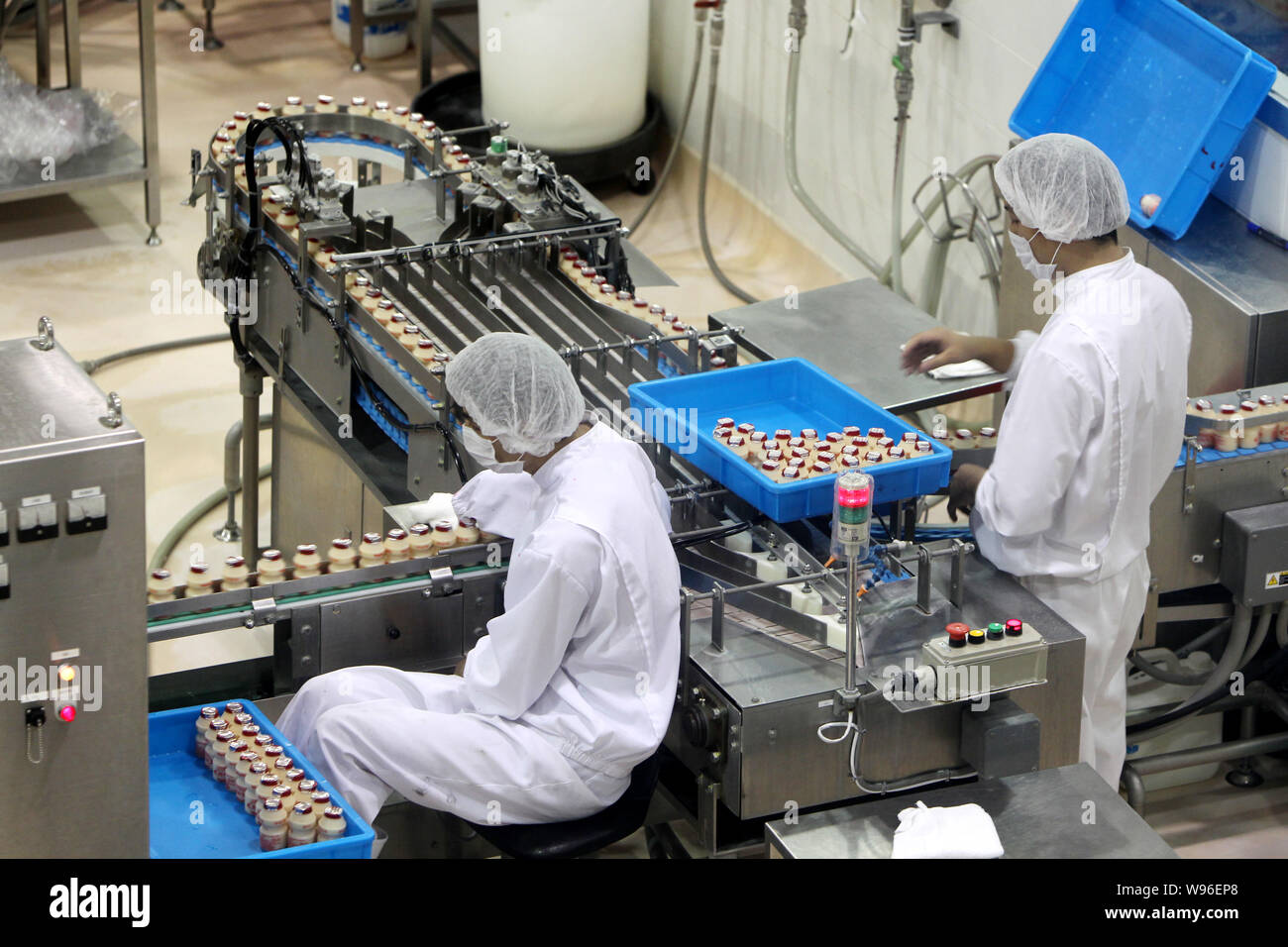 Factory workers watch bottles of Yakult fermented milk drink passing ...