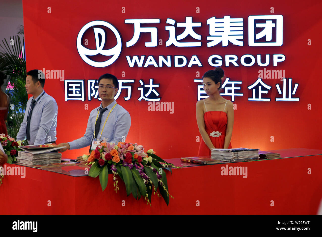 --FILE--Chinese staff members pose at the stand of Wanda Group during a ...