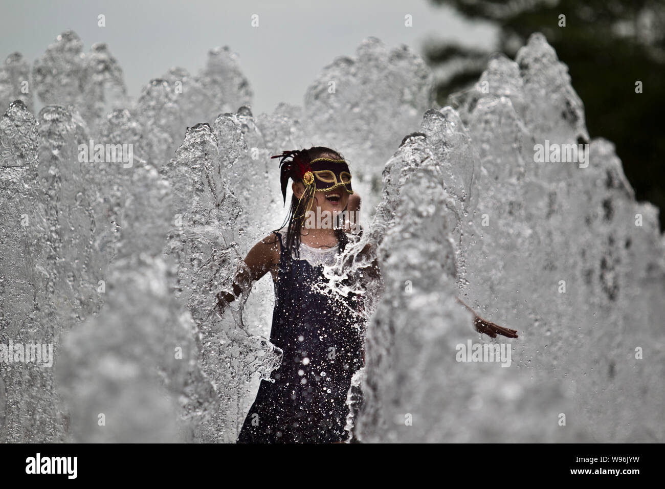 A girl plays with water to cool herself off in a hot day at a fountain ...