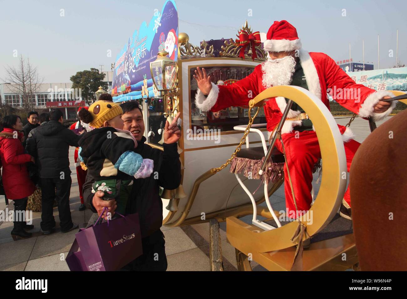 A young Chinese man dressed in a Santa Claus costume waves to ...