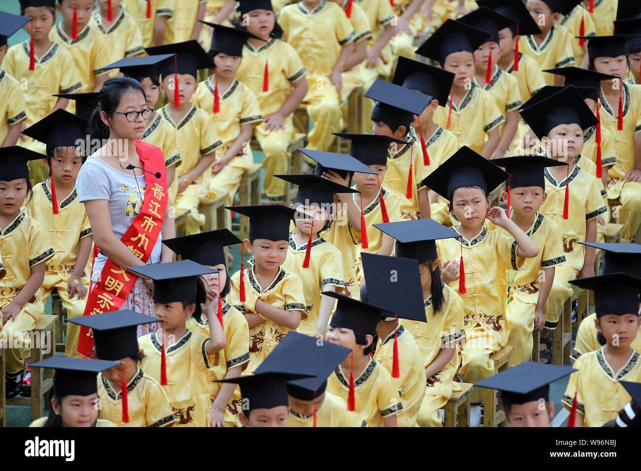 A Chinese teacher stands amongst rows of young Chinese students dressed ...