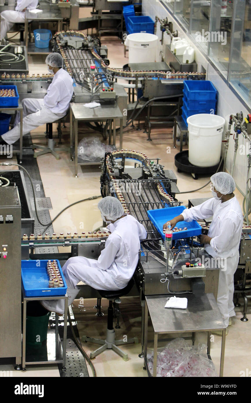 Factory workers watch bottles of Yakult fermented milk drink passing ...