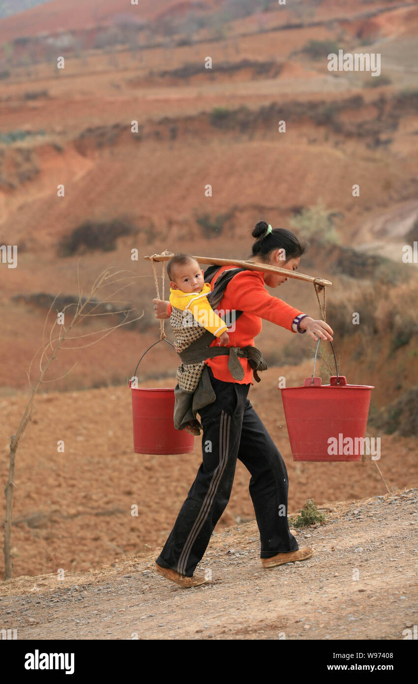 A Chinese woman carrying her child on the back shoulders buckets of ...