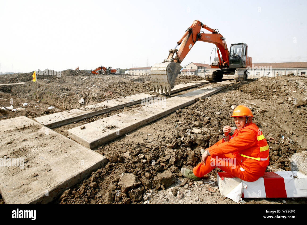 A Chinese worker rests next to an excavator digging the ground on the ...