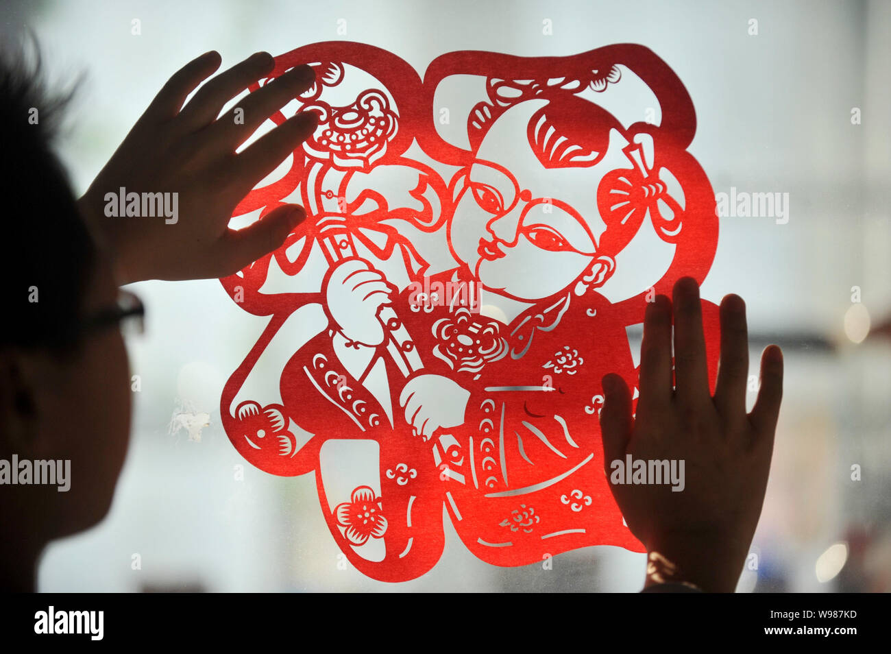 A local Chinese resident pastes a paper-cut work on the window in ...