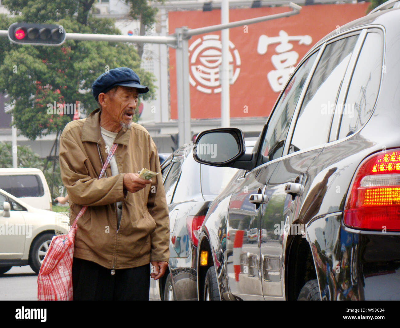 An elderly man begs for money car to car on a road in Dongguan city ...