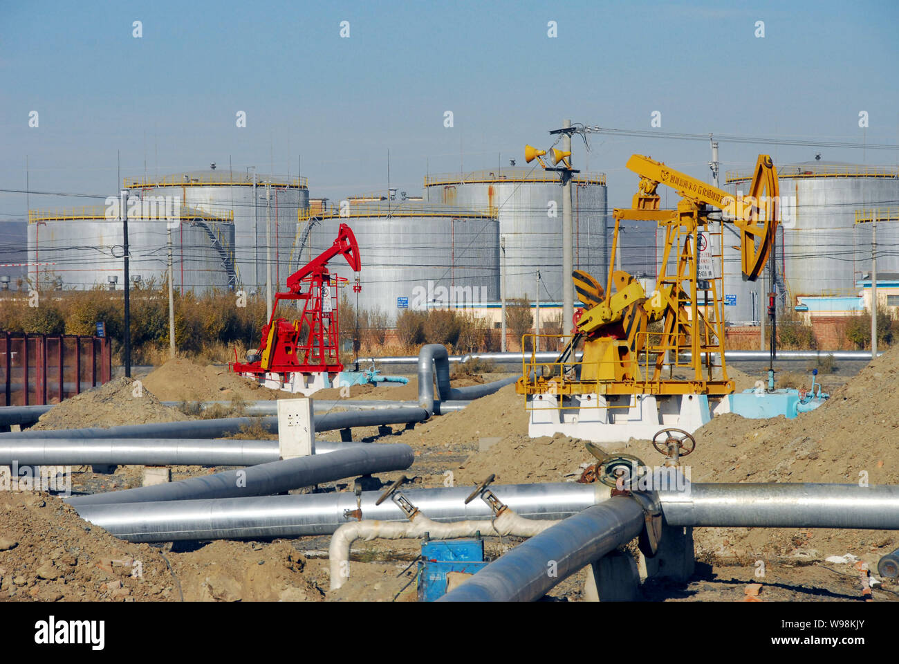--FILE--Derricks pump crude oil next to oil tanks in the Karamay oil ...
