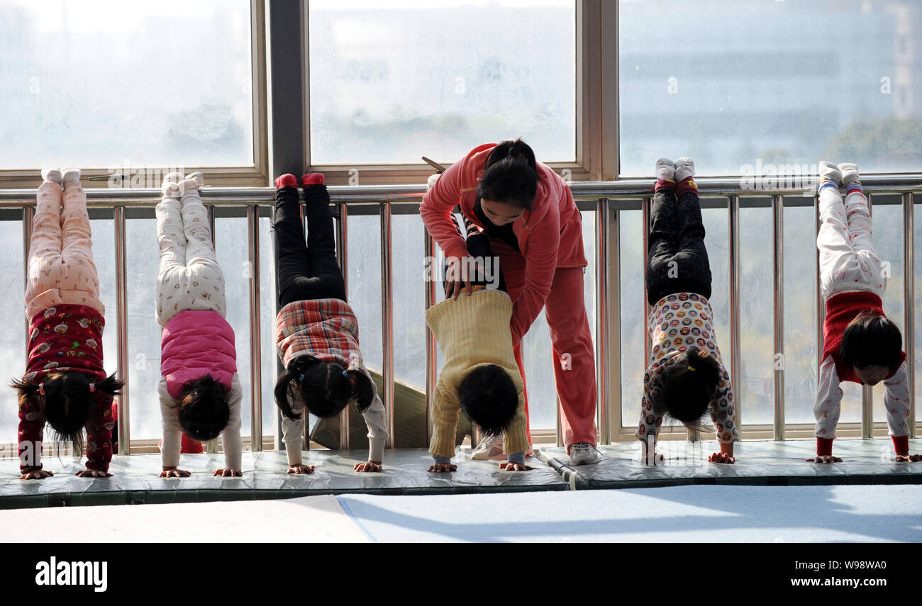 A coach adjusts the posture of a child hand-standing next to others ...