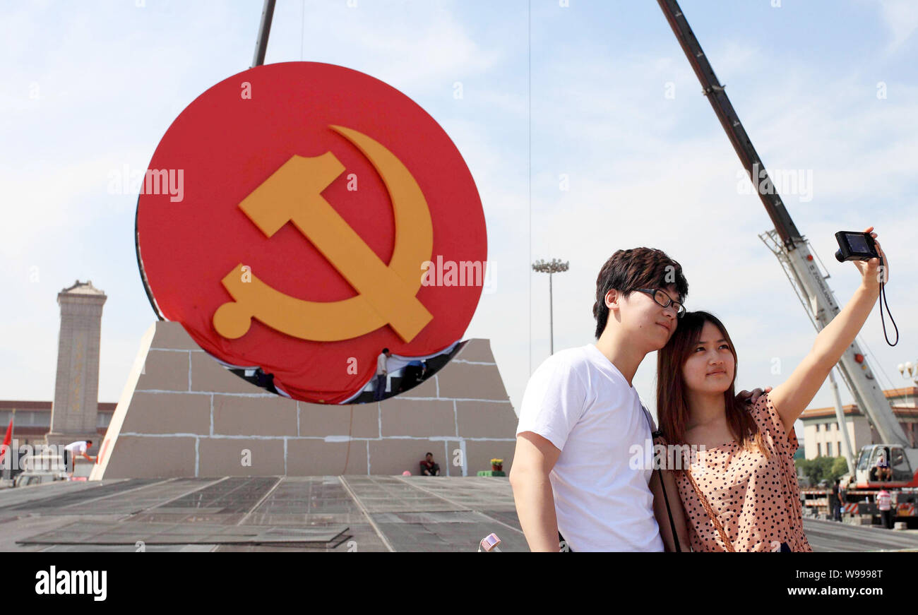 Tourists take photos in front of a huge emblem of the Communist Party ...