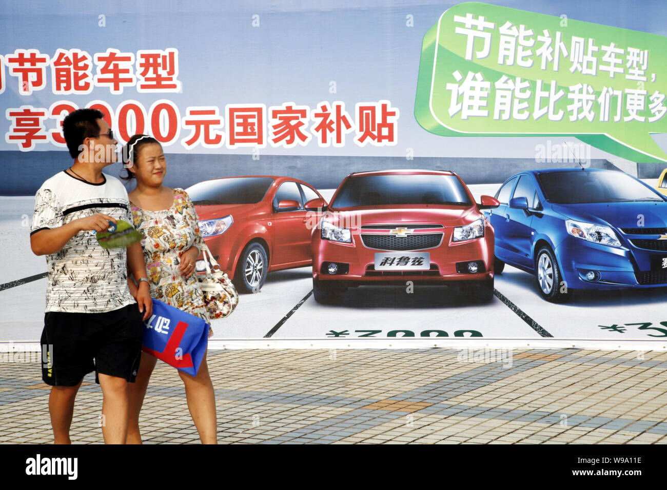 Chinese visitors walk past an advertisement for Chevrolet cars of ...